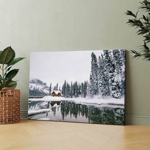 Картина на холсте (Домик стоит на заснеженном озере в окружении деревьев) 50x70 см. Интерьерная, на стену.